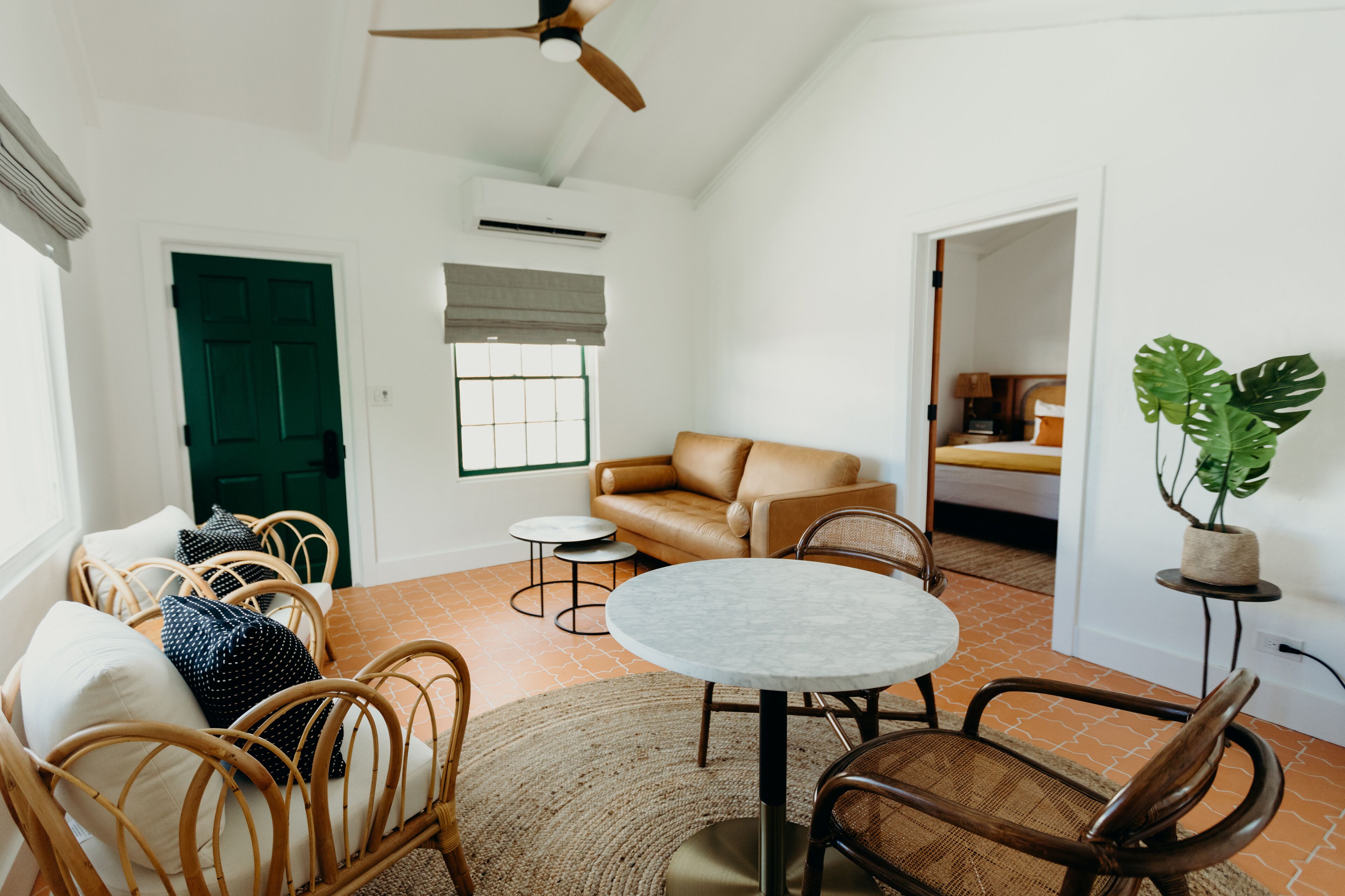 Uma sala de estar ampla, com mesa redonda, sofá de couro, cadeiras de vime e ventilador de teto.