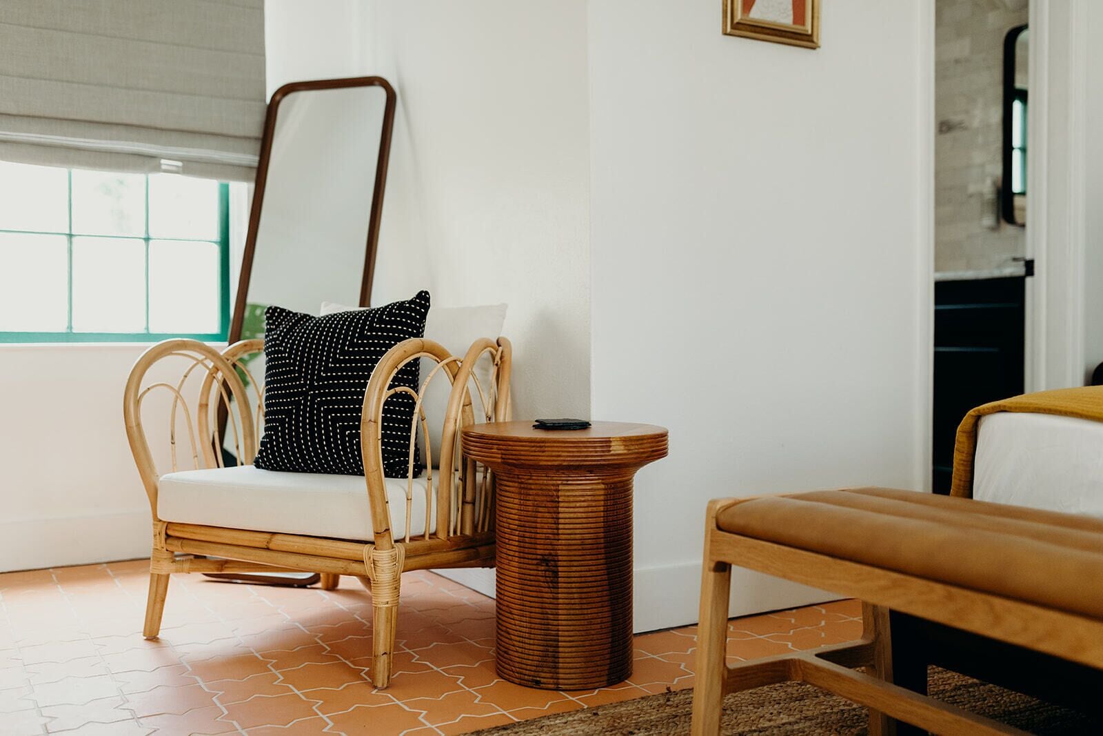 Um quarto com uma cadeira de vime, uma mesa redonda de madeira e um banco.