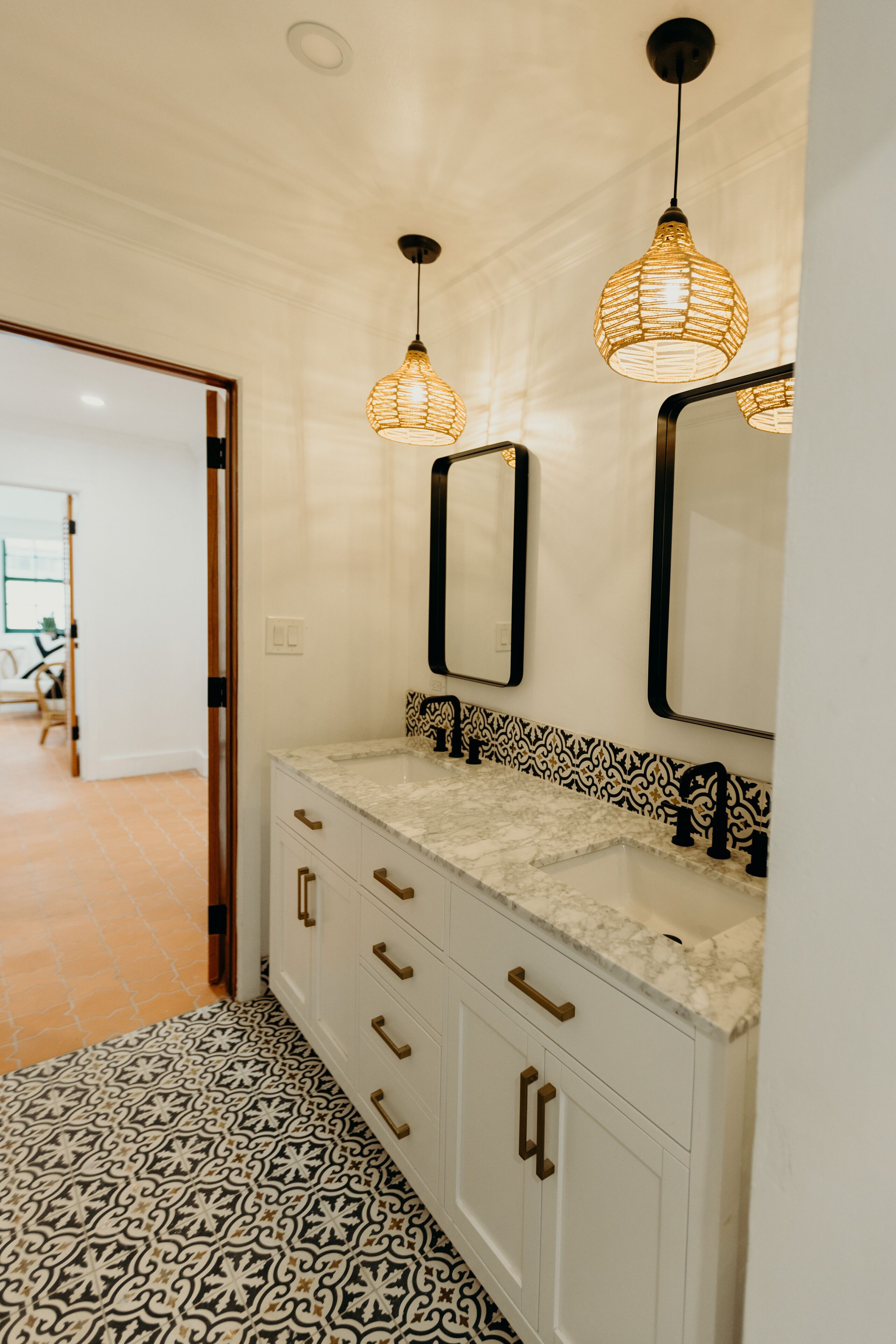 Casa de banho com toucador branco, azulejos com padrão preto e branco e duas luzes pendentes.