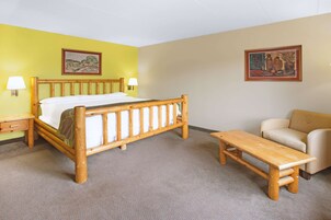 Quarto com cama de madeira, um banquinho de madeira, um sofá e duas luminárias fixadas na parede.
