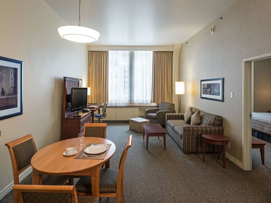 Quarto de hotel com área de refeições, sofá, televisão e cama.