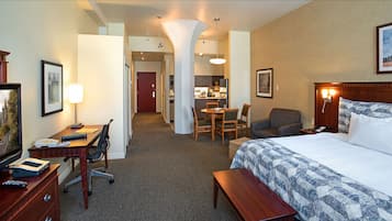 Quarto de hotel com cama, escrivaninha, cadeira e uma pequena cozinha.