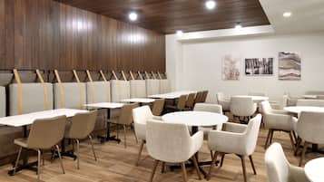 Uma sala de jantar moderna com áreas de cabine e mesas redondas, painéis de madeira nas paredes e obras de arte.