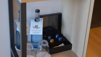 Minibar de quarto de hotel com cafeteira, duas chávenas, copos e uma garrafa de água.
