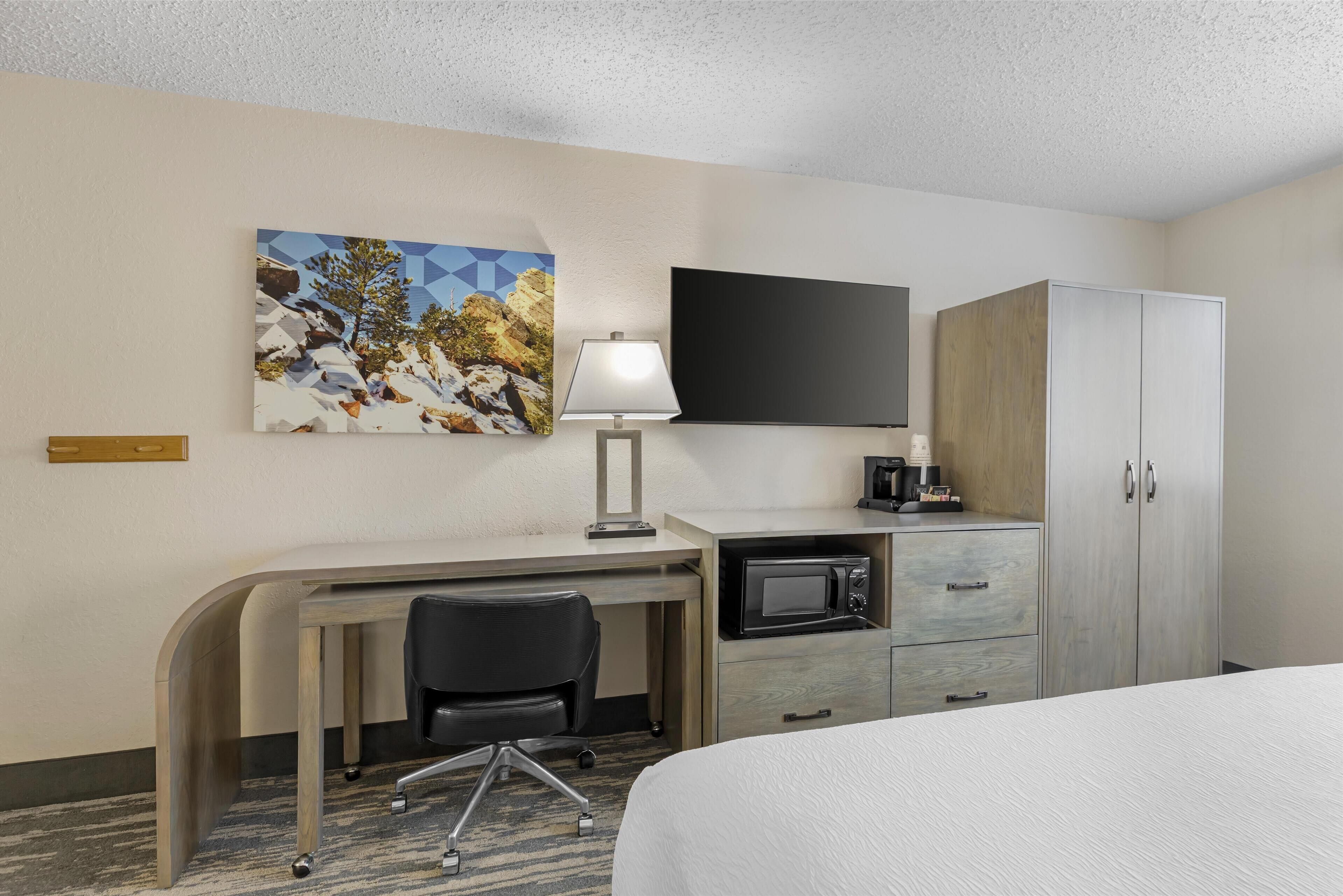 Quarto de hotel com cama, escrivaninha, cadeira, televisão, micro-ondas e armário.