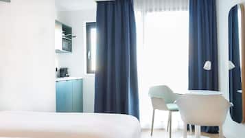 Quarto de hotel com uma cama, uma escrivaninha com cadeira, um espelho e uma janela com cortinas.