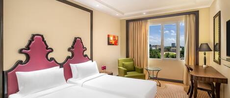 Quarto de hotel com uma cama grande, uma escrivaninha, uma cadeira e vista para a cidade.