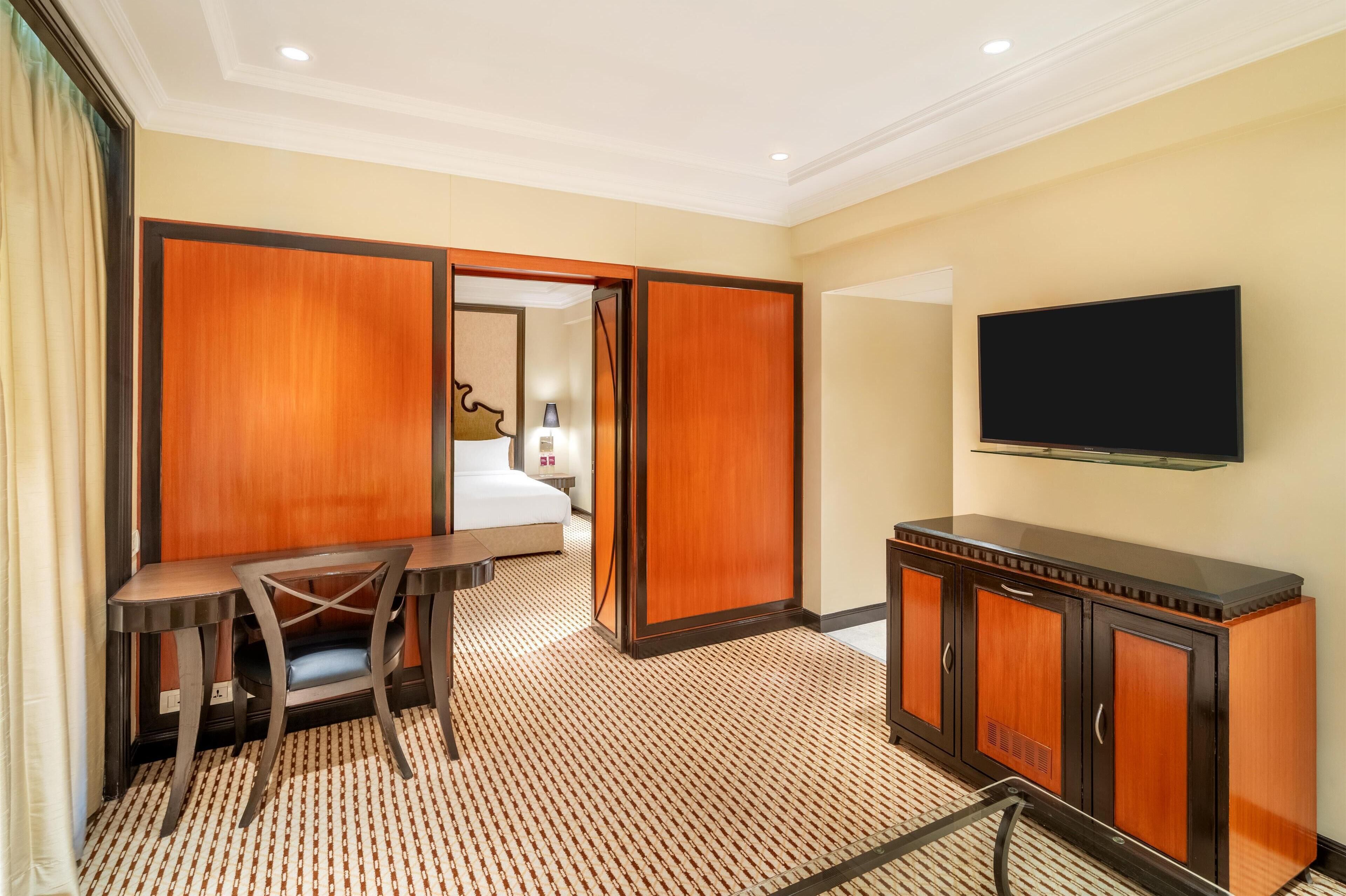 Quarto de hotel com uma cama, uma escrivaninha com cadeira, televisão e guarda-roupa.