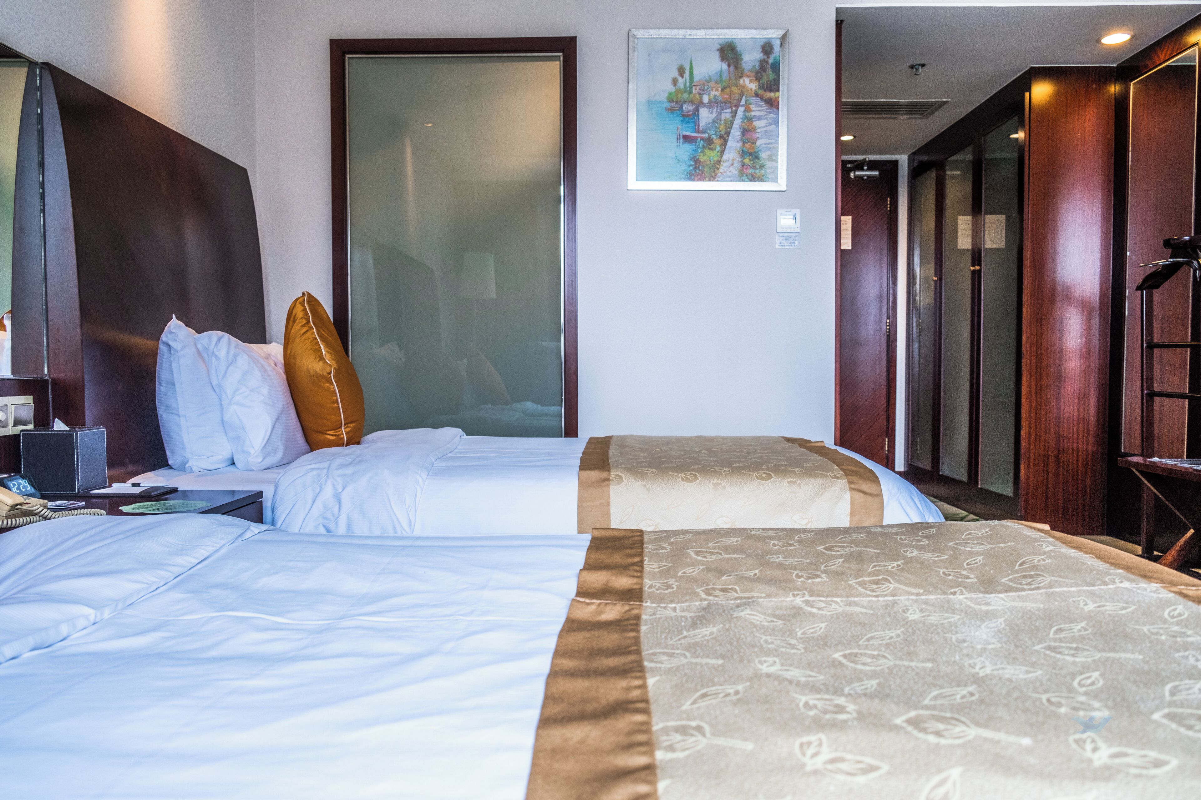 Quarto de hotel com duas camas, uma mesa de trabalho e um telefone, e um quadro na parede.