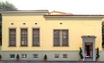 Um edifício com fachada amarela, três janelas com grades de metal e uma porta com pequeno alpendre.