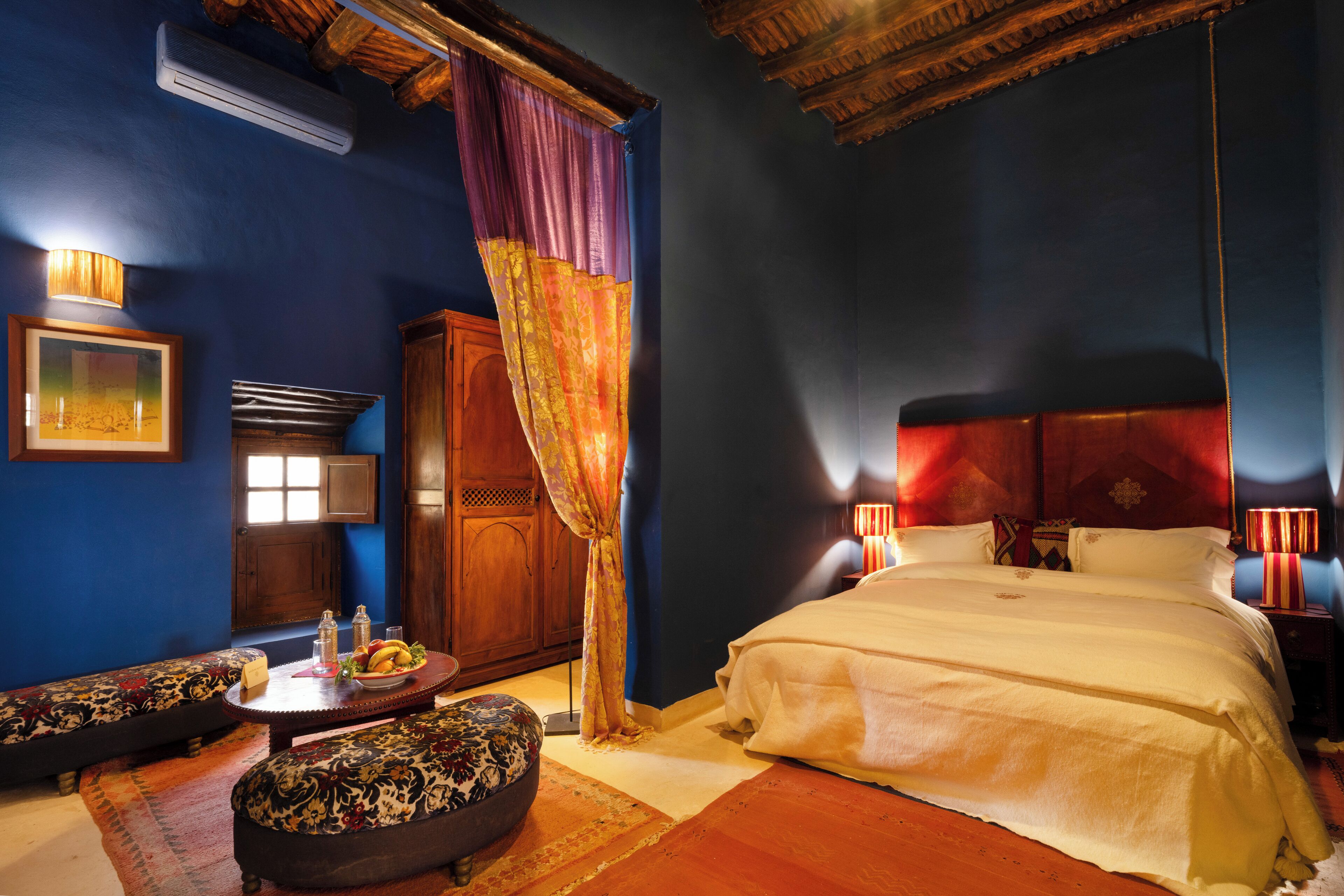 Quarto com cama grande, guarda-roupa de madeira, um banquinho e uma mesa com uma fruteira.