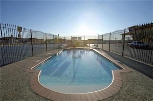 Piscina retangular com borda de tijolos, cercada por uma grade preta.