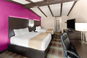 Quarto de hotel com duas camas, uma mesa com televisão e uma cadeira.