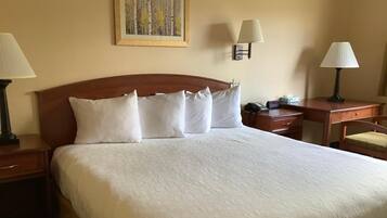 Quarto de hotel com uma cama grande, duas mesas de cabeceira, uma escrivaninha com cadeira e duas luminárias fixadas na parede.