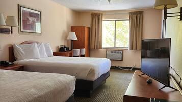 Quarto de hotel com duas camas, uma escrivaninha com televisão, uma luminária e um quadro na parede.