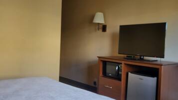 Quarto de hotel com uma cama, televisão em um armário de madeira, micro-ondas e geladeira.