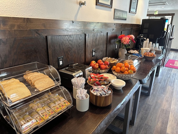 Uma área de buffet com diversos alimentos, incluindo pães, frutas e acompanhamentos.