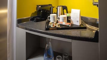 Cozinha compacta de hotel com cafeteira, chaleira e bandeja com xícaras de café e acompanhamentos.