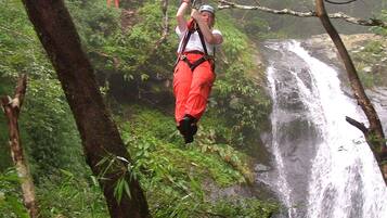 Uma pessoa praticando tirolesa em meio a uma floresta, com uma cachoeira ao fundo.