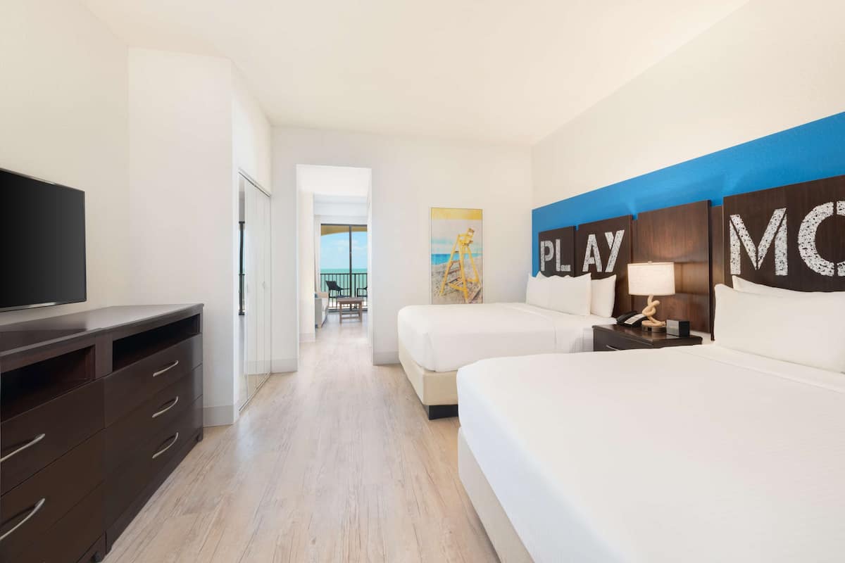 Quarto de hotel com televisão, cama, mesa de cabeceira e um quadro na parede.