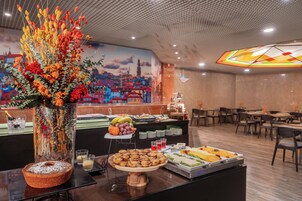 Uma área de buffet com diversas opções de comida, um vaso decorativo e um mural com vista para a cidade na parede.