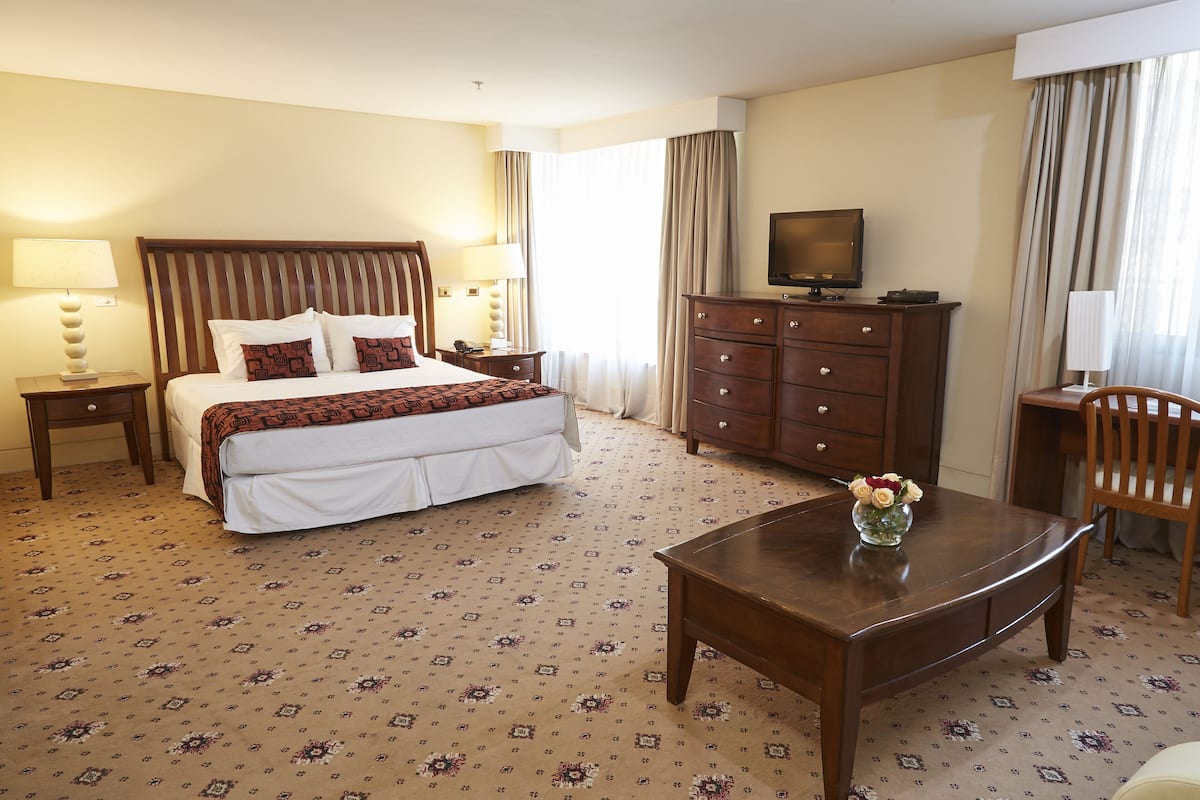 Quarto de hotel com cama, cómoda de madeira, televisão, secretária e uma cadeira.