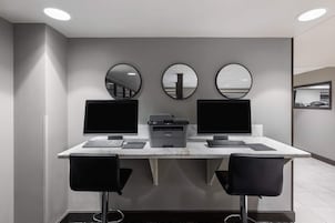 Um espaço de escritório moderno com duas mesas, cada uma com monitor, teclado e rato. Há três espelhos redondos na parede e uma impressora entre as mesas.