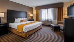 Quarto de hotel com cama grande, escrivaninha, cadeira, televisão e janela com cortinas.