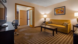 Quarto de hotel com escrivaninha, cadeira de escritório, sofá e duas luminárias.