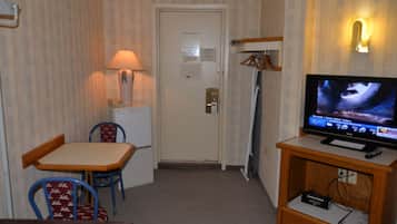 Quarto de hotel com televisão, uma mesinha e duas cadeiras, um abajur e um porta-roupas.