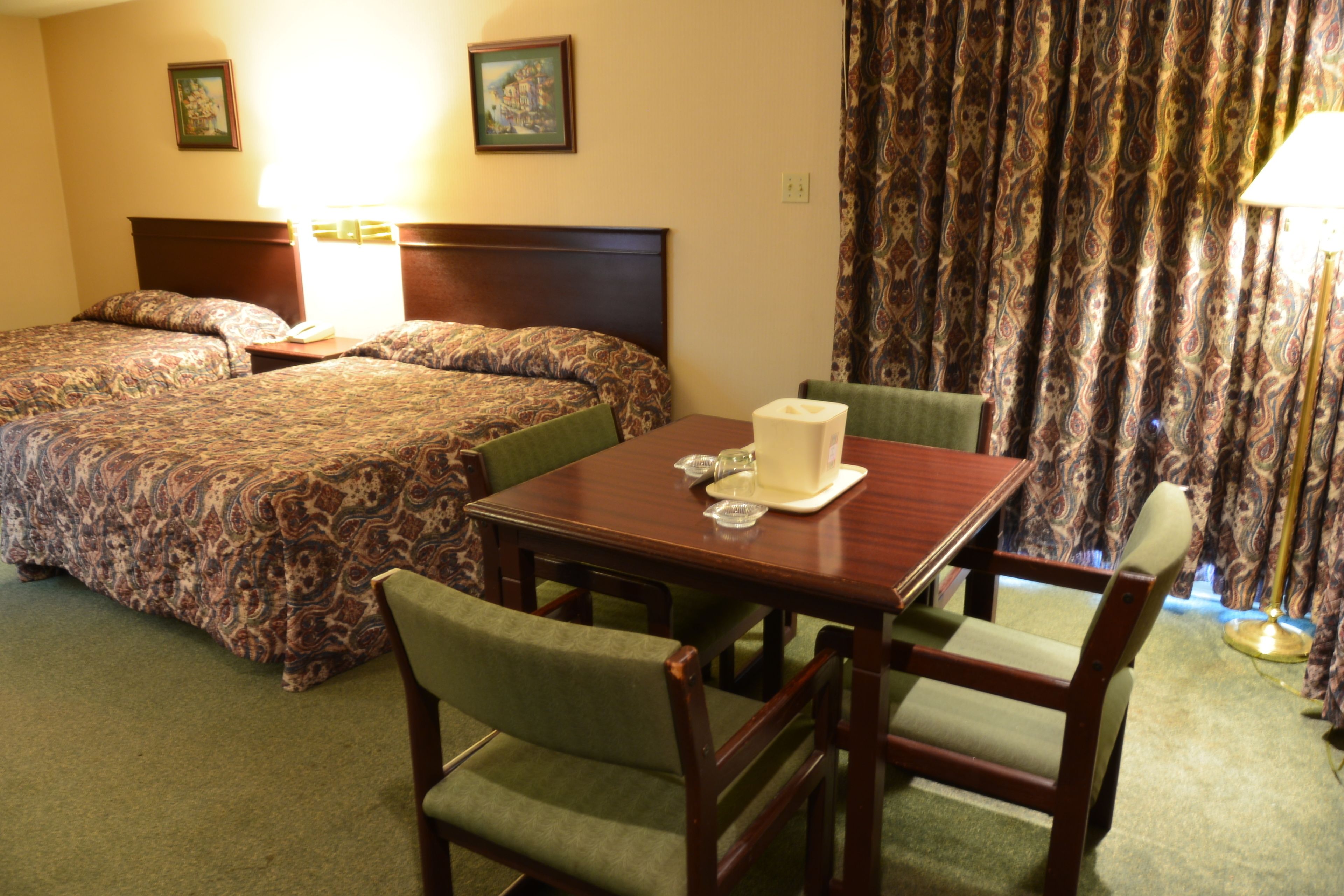 Quarto de hotel com duas camas, uma mesa de jantar com cadeiras e um abajur.