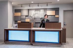 Uma receção de hotel com design moderno, incluindo um ecrã digital e a placa da Holiday Inn Express & Suites.