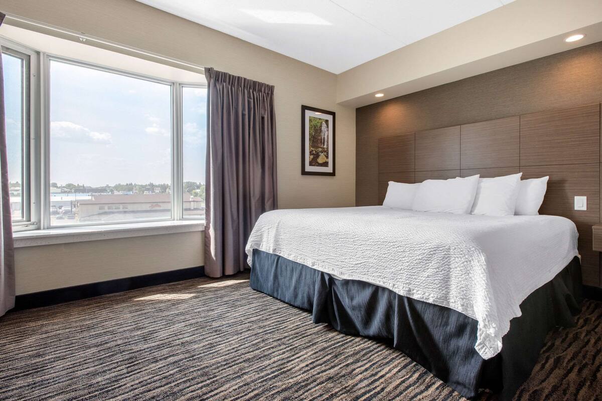 Quarto de hotel com uma cama grande, vista para a cidade e uma janela com cortinas.