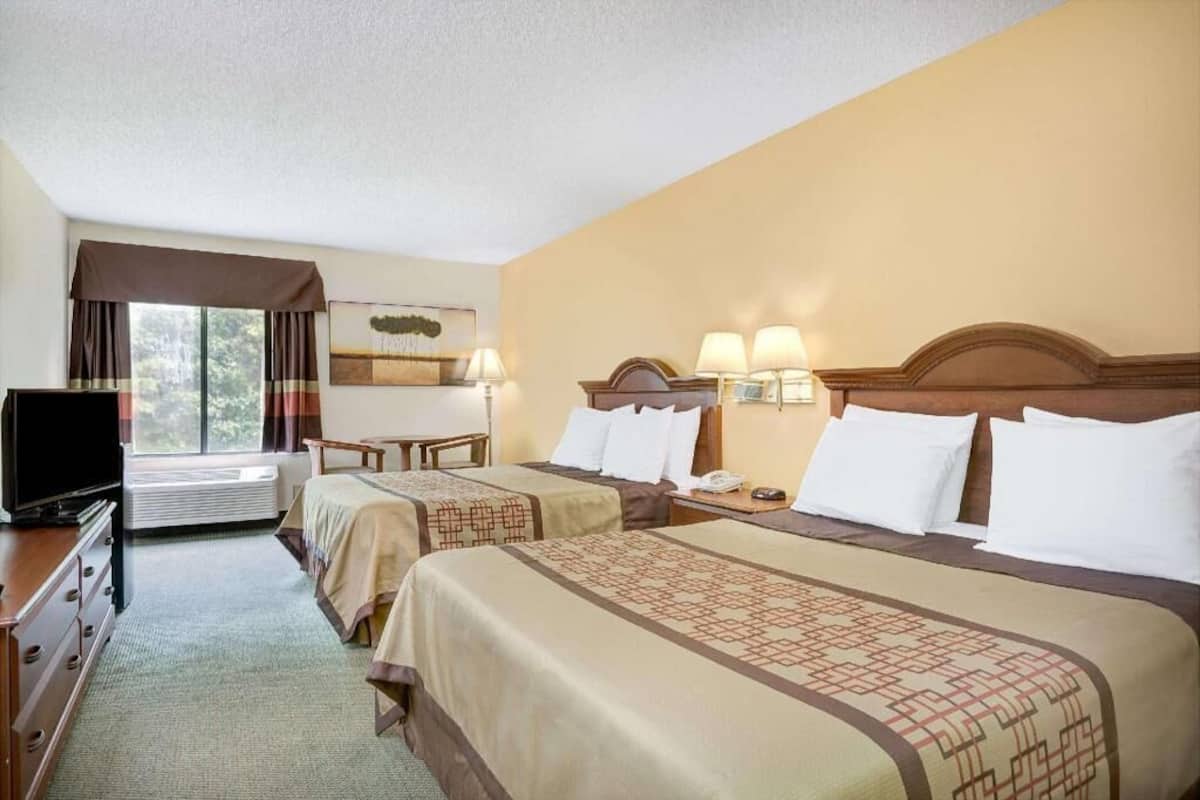 Quarto de hotel com duas camas, televisão, escrivaninha e janela com cortinas.