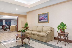Uma sala de estar com um sofá, duas mesas laterais com plantas em vasos, uma mesa de centro e um quadro na parede.