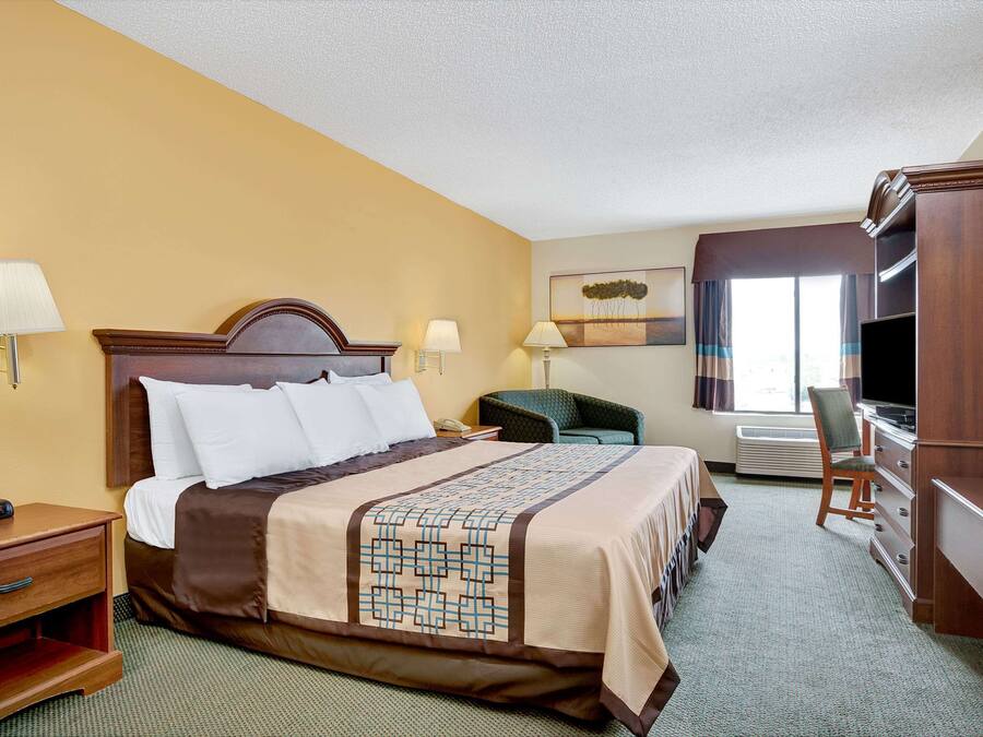 Quarto de hotel com uma cama grande, luminárias de cabeceira, escrivaninha, cadeira, televisão e cômoda.