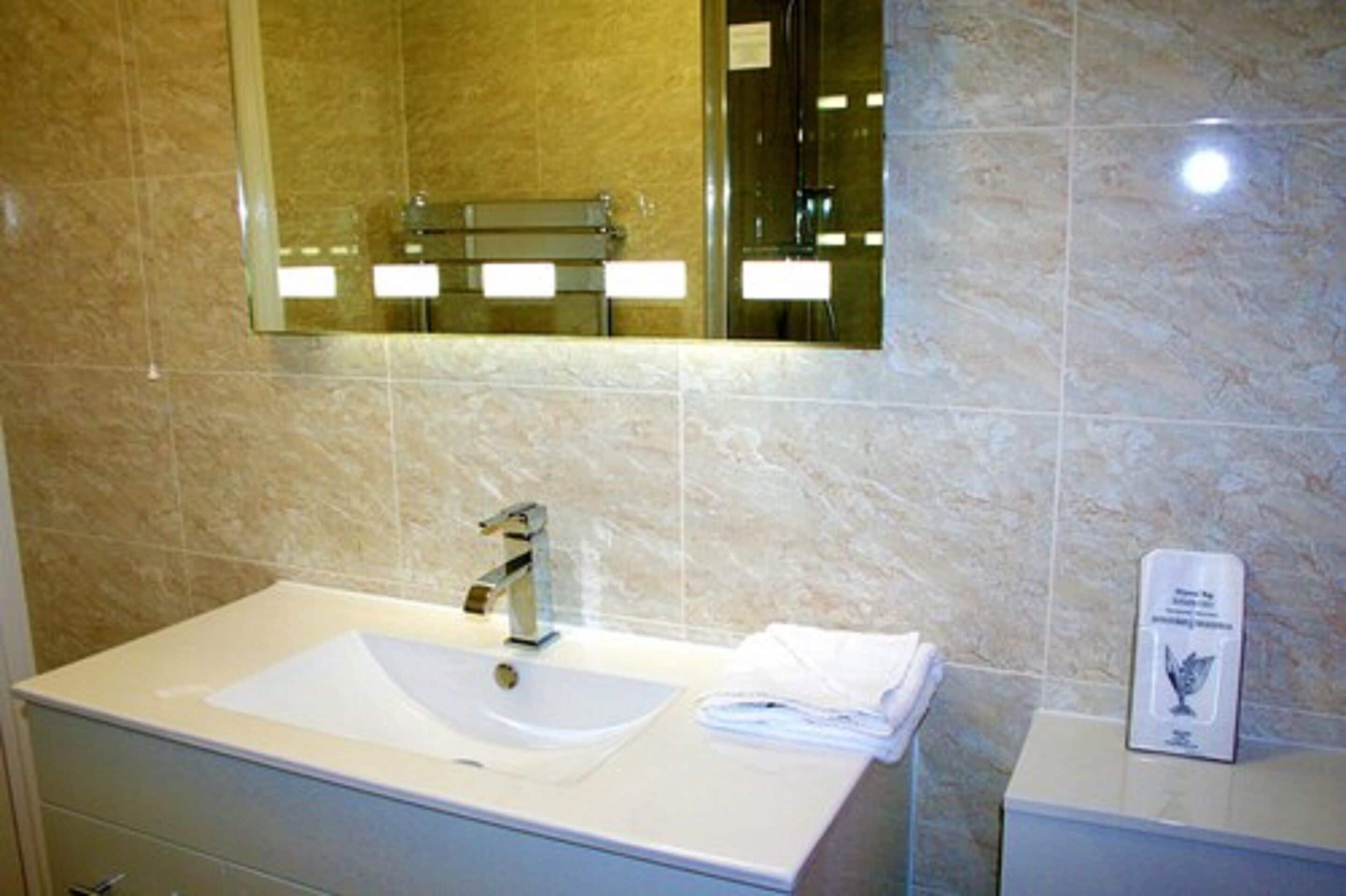 Casa de banho com lavatório branco, espelho e porta-toalhas.