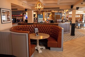 Um restaurante acolhedor com área de bar, espaço para café self-service e área de estar com mesa redonda e banco acolchoado.