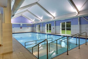 Piscina interior com água azul cristalina, rodeada por paredes revestidas de azulejos e uma barreira de vidro.