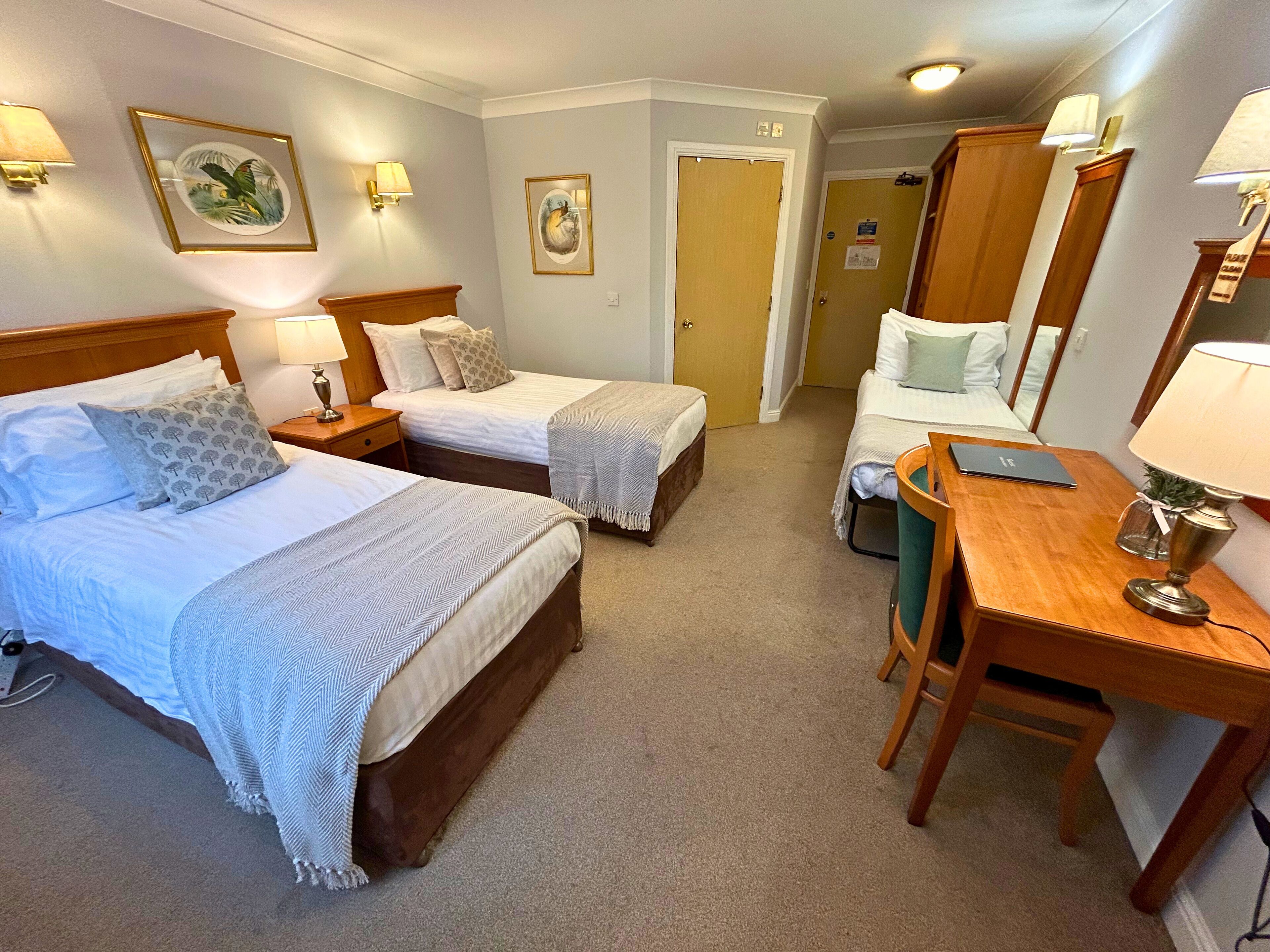 Quarto de hotel com duas camas de solteiro, uma escrivaninha de madeira, um laptop e um espelho.