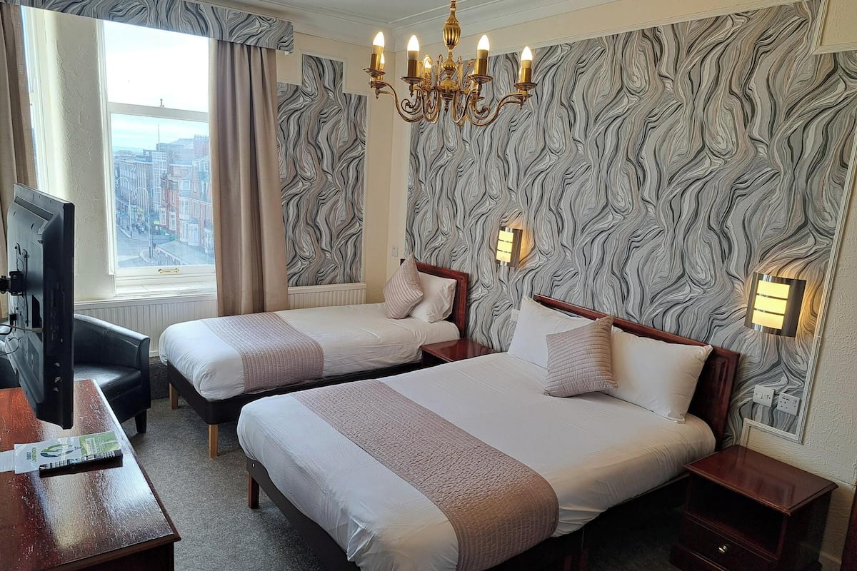 Quarto de hotel com duas camas, televisão, secretária e vista para a cidade.