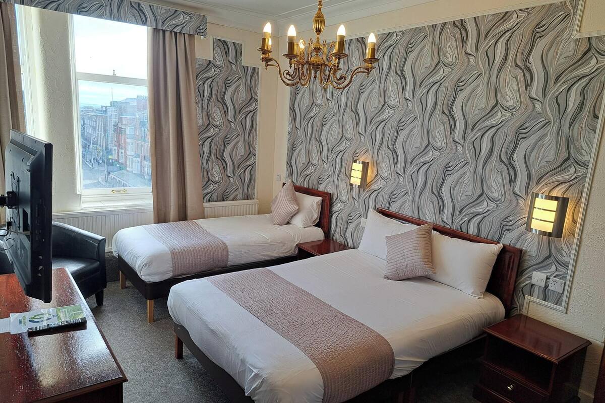 Quarto de hotel com duas camas, televisão, secretária e vista para a cidade.