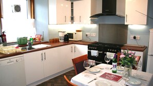 Uma cozinha compacta com armários brancos, fogão preto e uma mesa de jantar posta para dois, com copos de vinho e um cardápio.