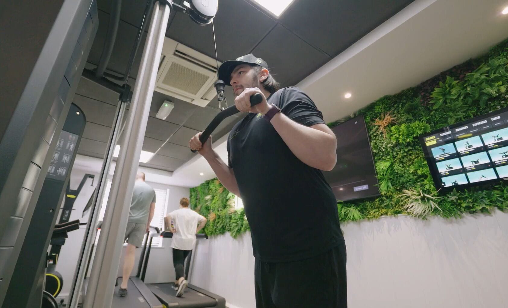 Uma academia com equipamentos de exercício, uma televisão na parede e uma pessoa usando uma bicicleta ergométrica.