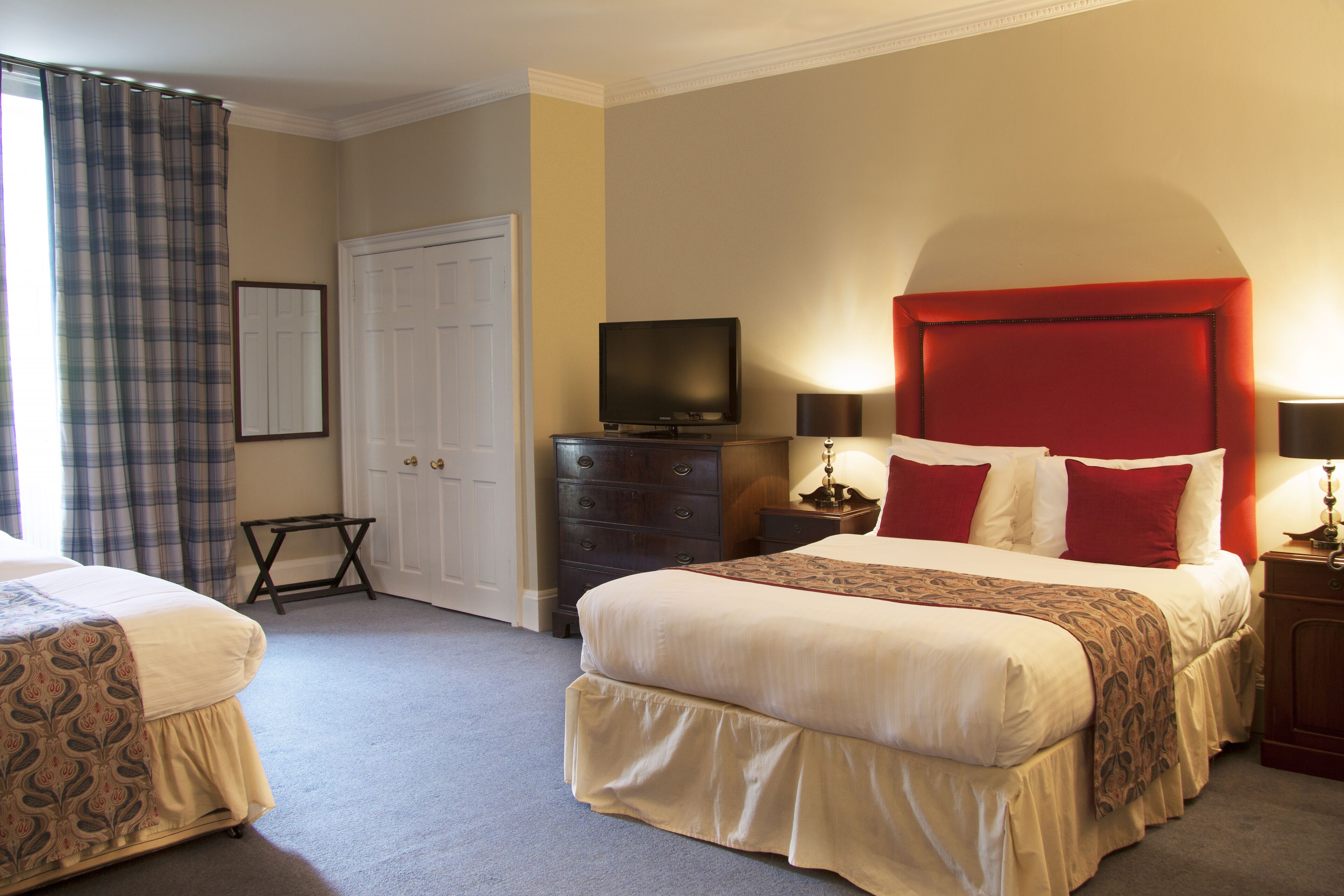 Quarto de hotel com uma cama grande, uma cama menor, uma televisão, uma cômoda e uma porta.