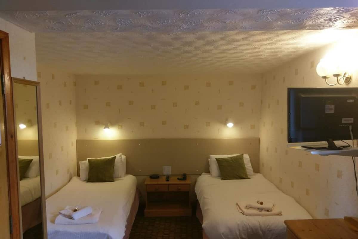 Quarto de hotel com duas camas, uma televisão, um espelho e uma mesinha.
