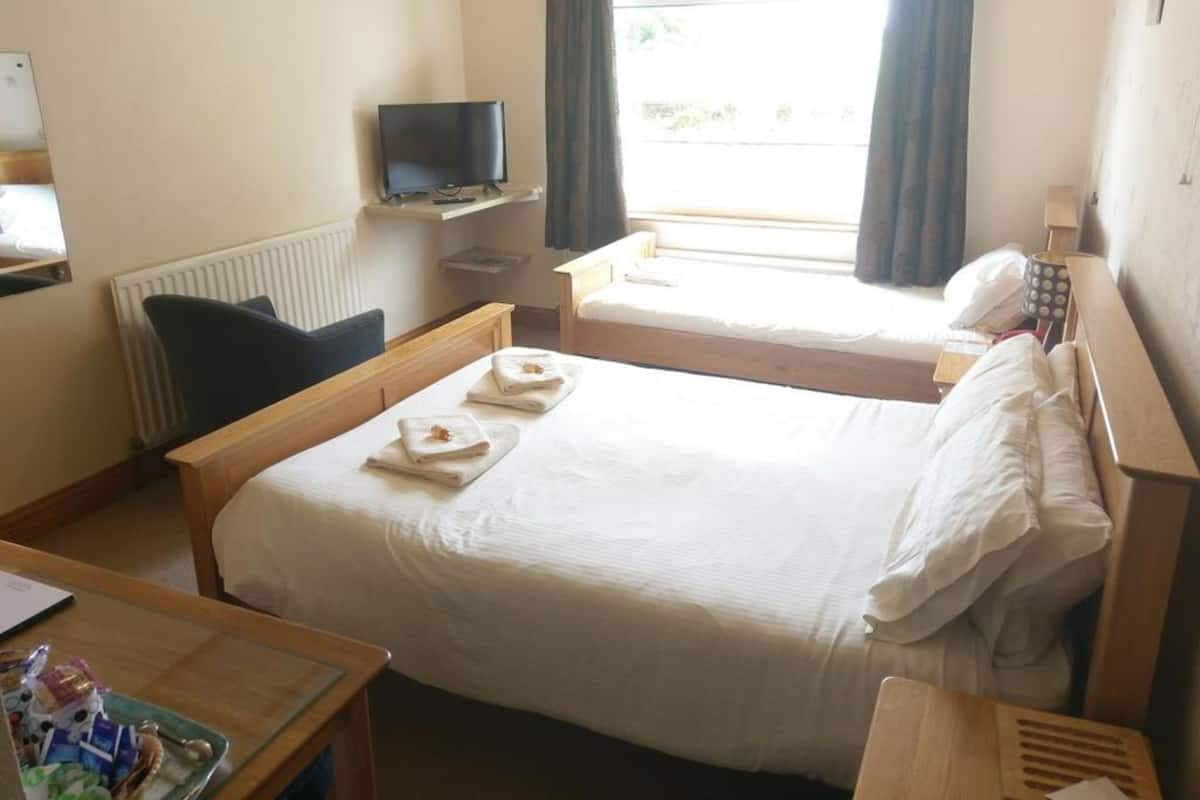 Quarto de hotel com duas camas, televisão, escrivaninha e janela com cortinas.