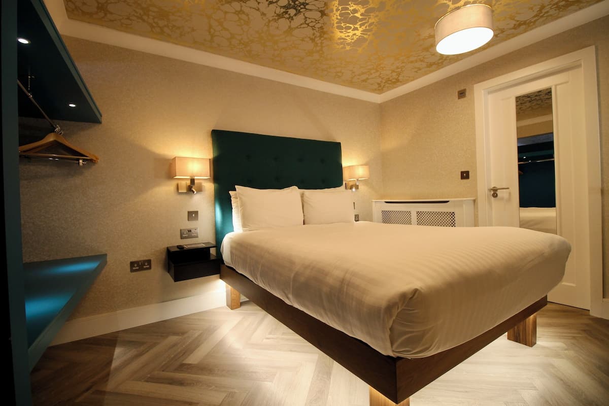Quarto com cama grande, luminárias laterais, guarda-roupa e cabideiro.