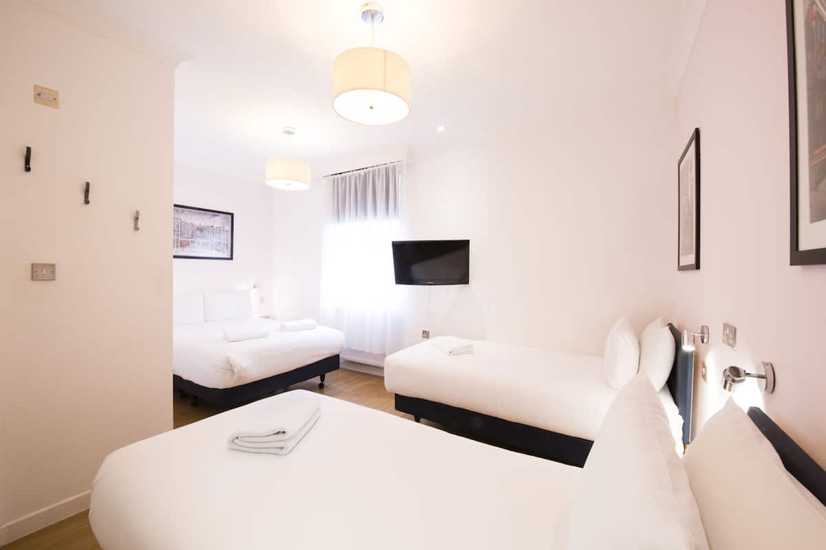 Quarto de hotel com duas camas, televisão de tela plana e uma grande janela com cortinas.