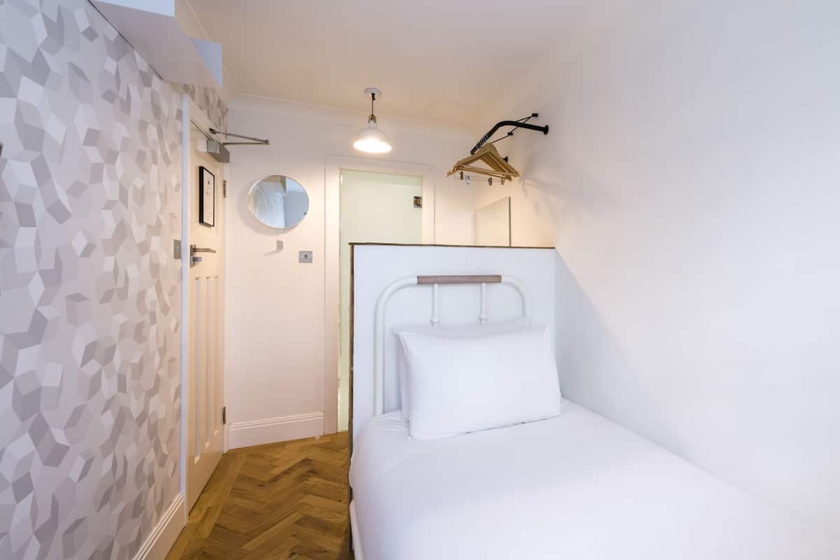 Um quarto pequeno e moderno com uma cama, uma mesa de cabeceira, um espelho e uma parede com padrão geométrico.